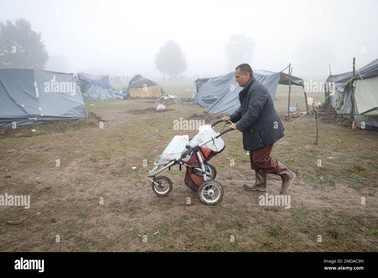 A migrant man carries drinking water in a baby stroller at a makeshift ...