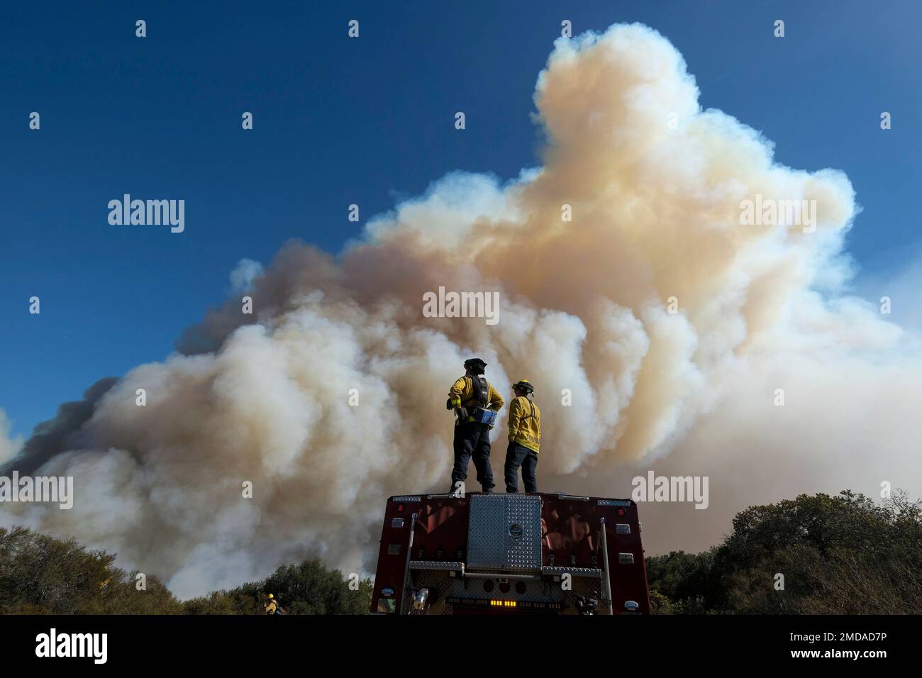 Firefighters watch on their fire engine as smoke rises from a wildfire ...