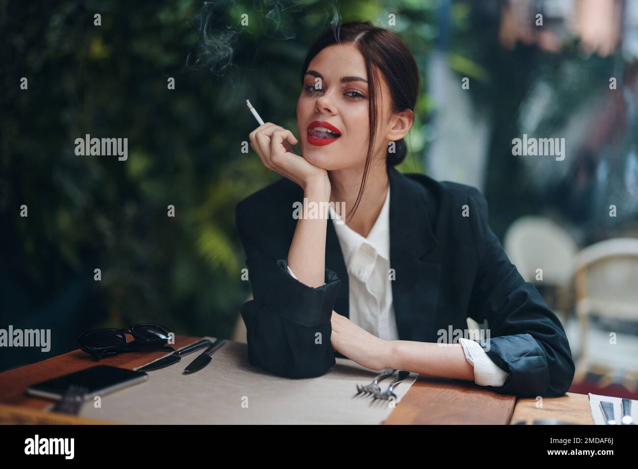 Stylish fashion woman sits in a cafe at a table and smokes a cigarette ...