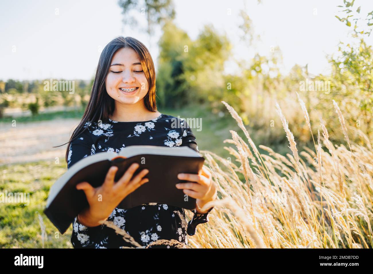 Innocent young religious girl with braces studying the bible, outside ...