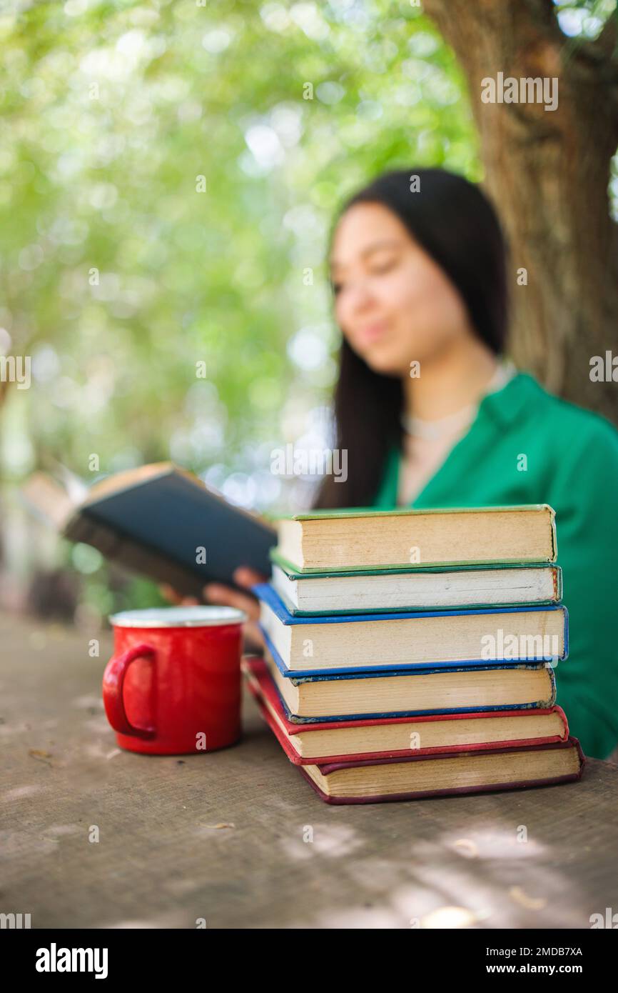 Defocused young woman reading stacked books in the field under a willow ...