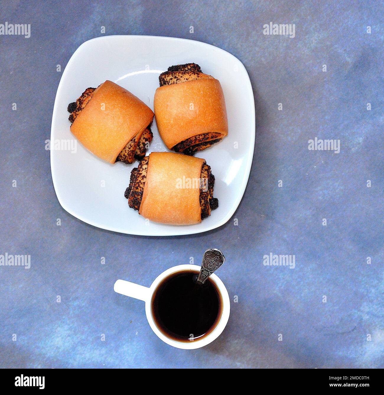 Three fresh poppy seed buns on a porcelain plate and a cup of hot black ...