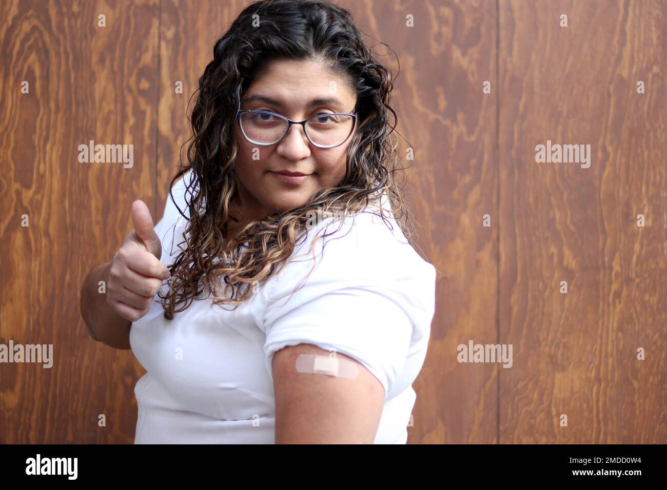 Latin adult woman with white blouse wavy hair and glasses shows her arm ...