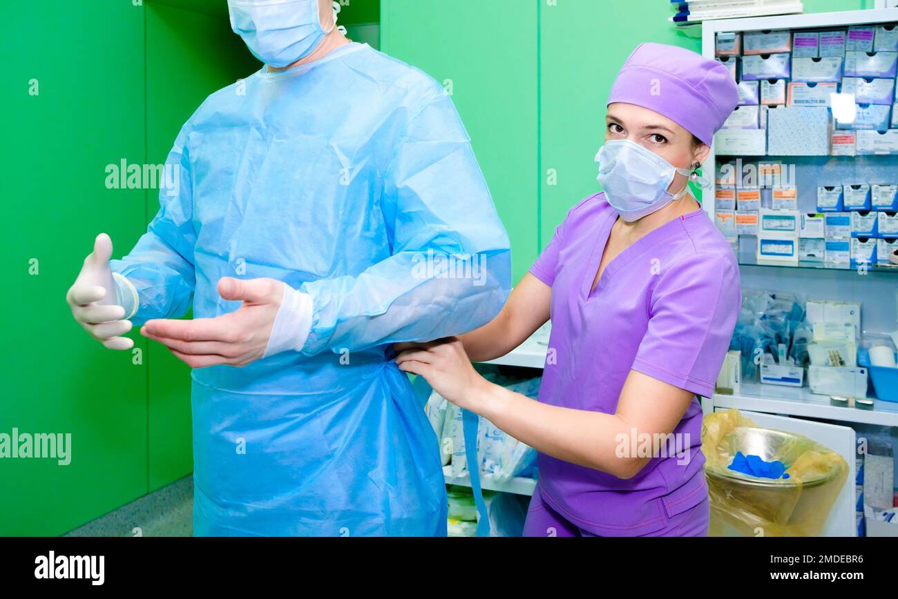A nurse in the operating room helps the surgeon dress in a sterile ...