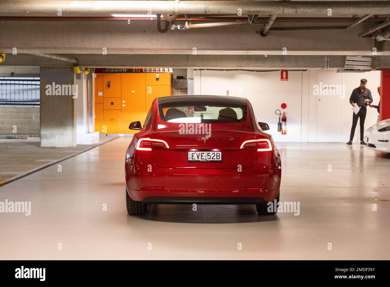 red Tesla model 3 driving away by new owner from collection bay at ...