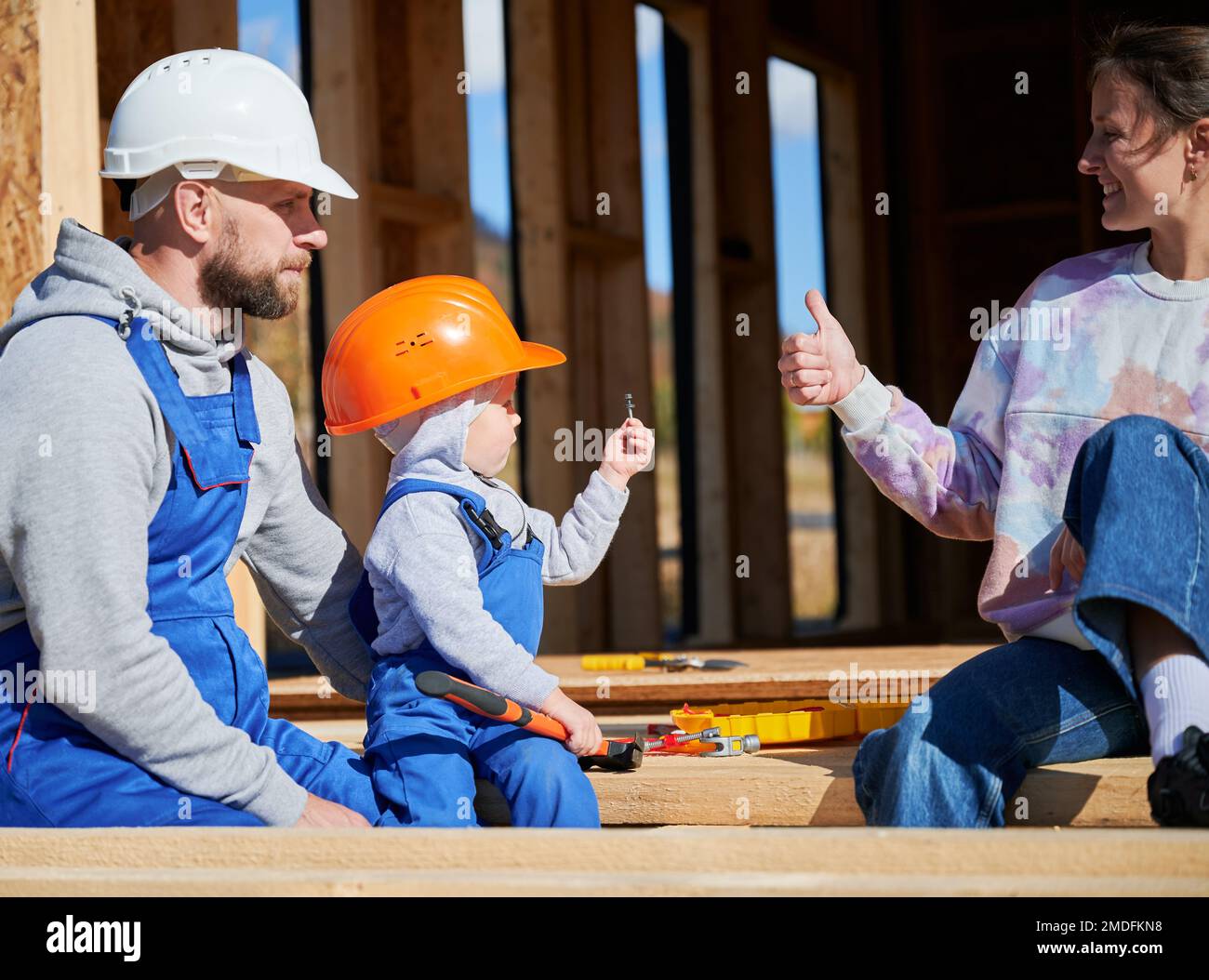 Father, mother and son building wooden frame house. Toddler boy helping ...