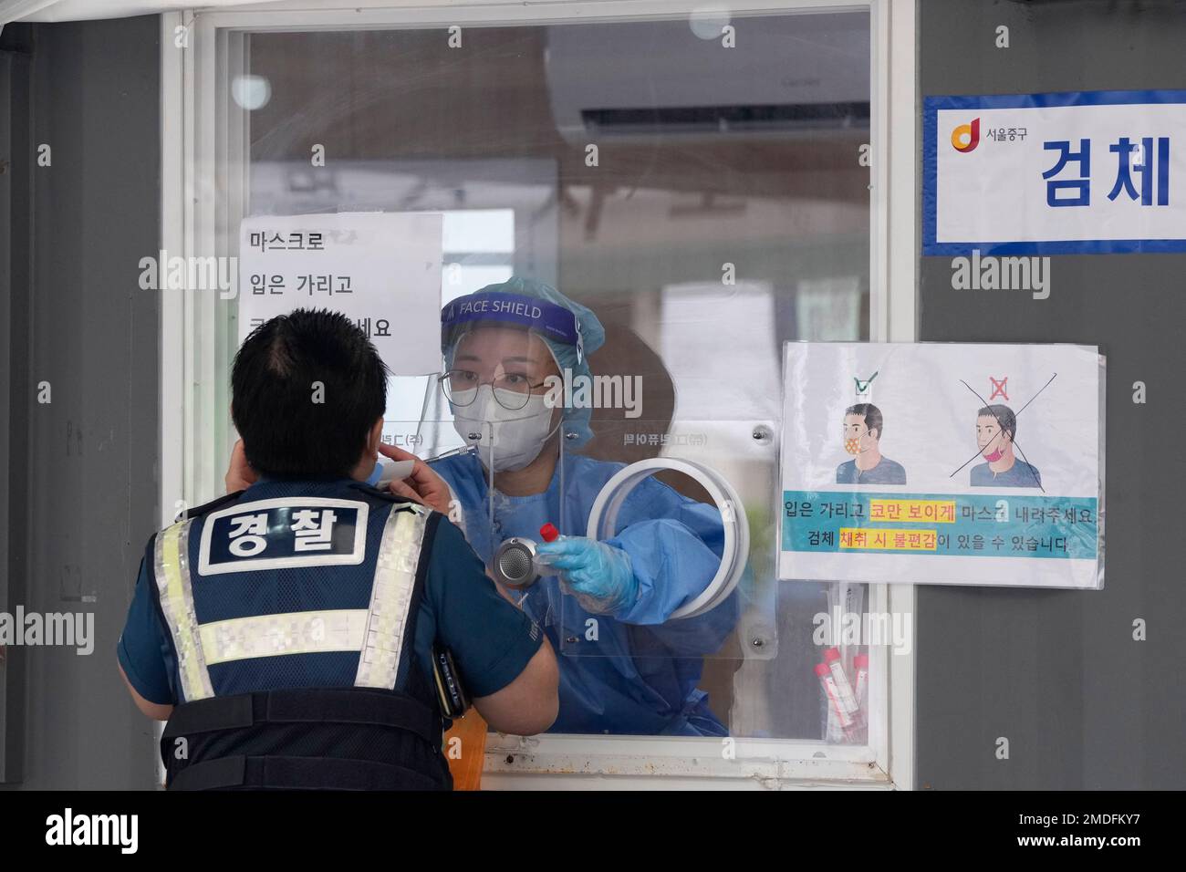 A medical worker in a booth takes a nasal sample from a police officer ...