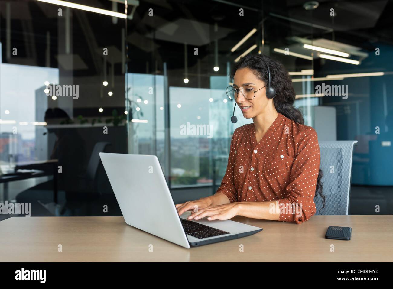 Smiling hispanic businesswoman working inside office with laptop and ...