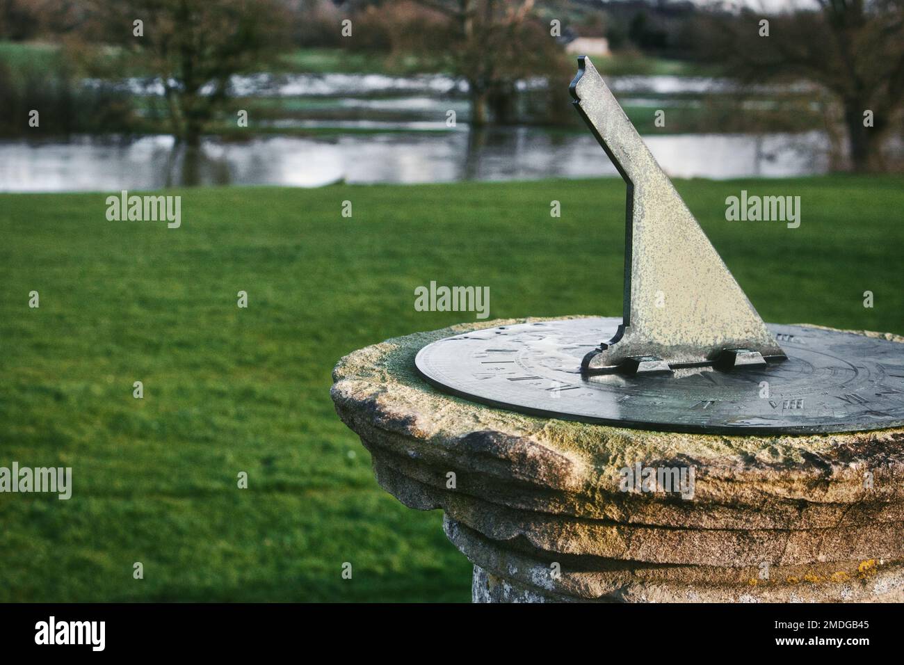 An old metal sundial set on a stone plinth or pedestal on a grassy lawn ...