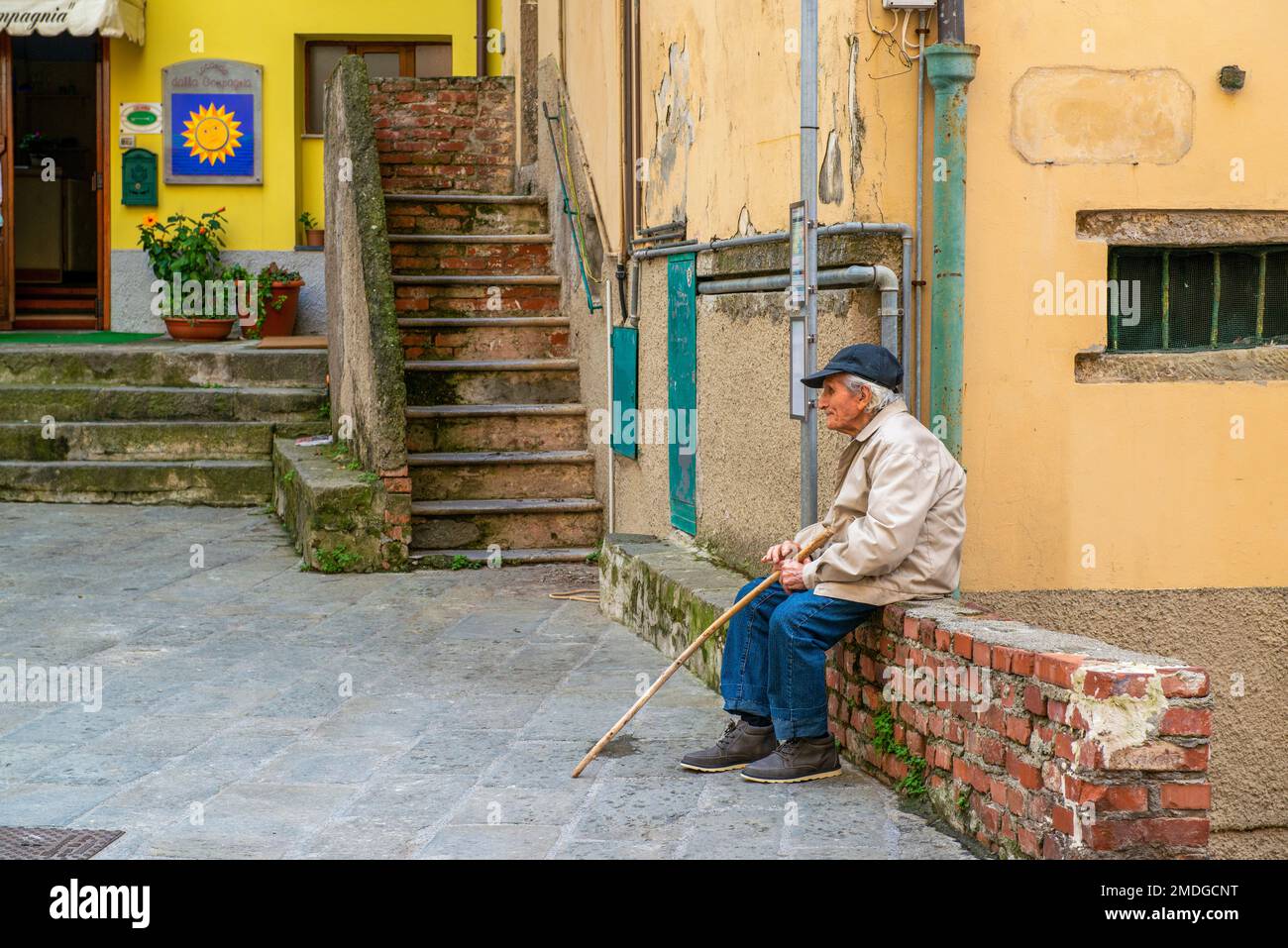 an old man sitting resting on a stone wall, Italy Stock Photo - Alamy