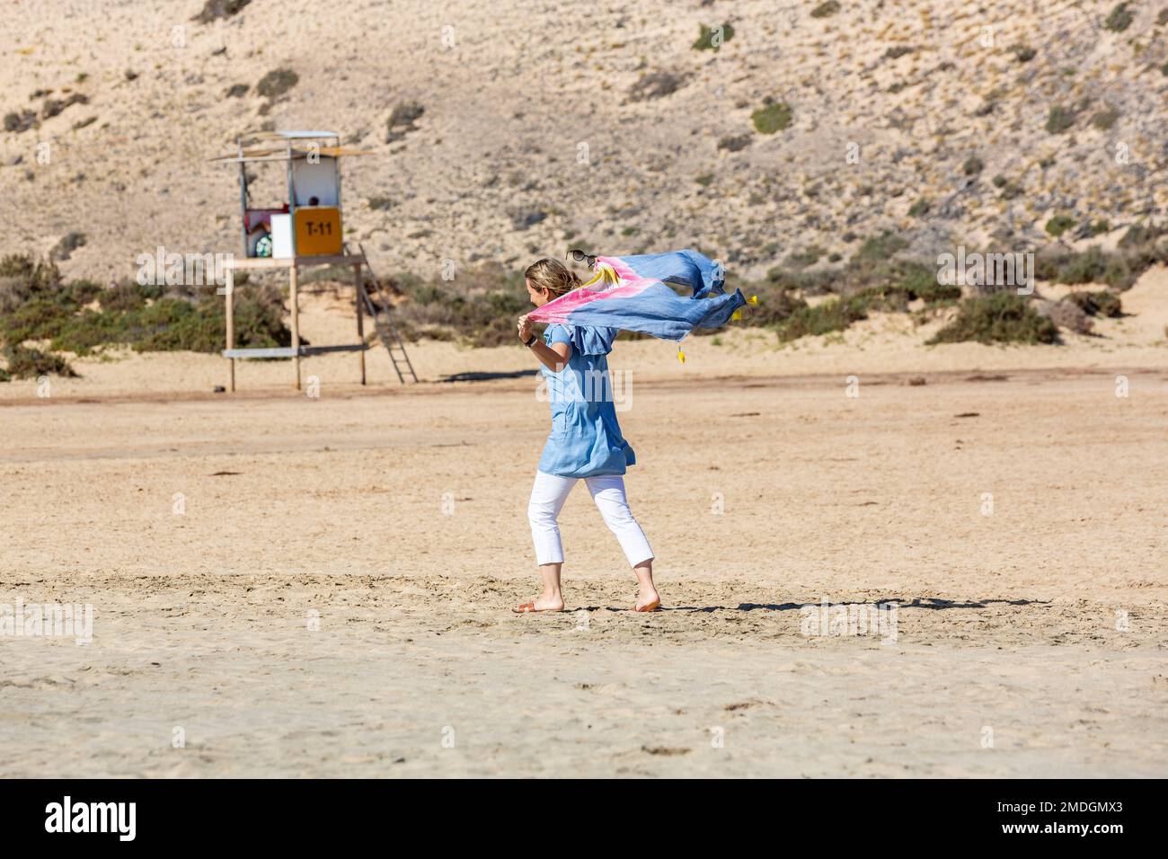 Young woman walking against the wind on Sotavento beach, her coat ...