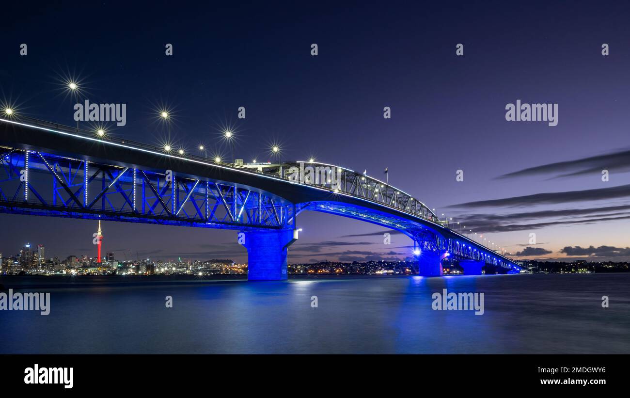 Auckland Harbour Bridge glowing in blue. Skytower in gold and red ...