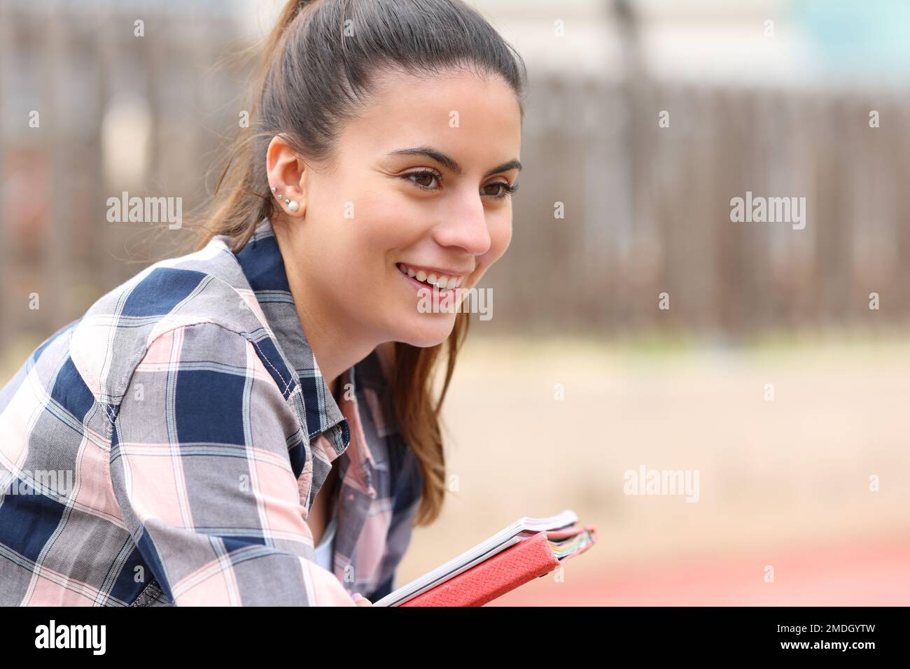 Portrait of a happy student looking away sitting in a park Stock Photo ...