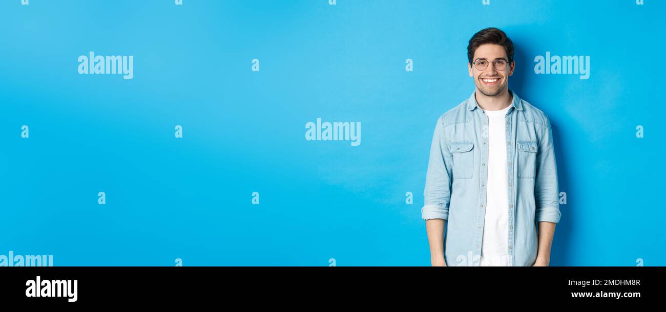 Young modern man in glasses and casual outfit standing against blue ...