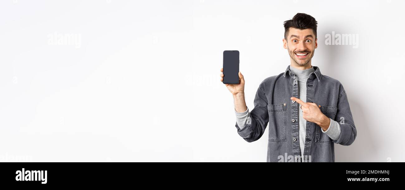 Handsome smiling man pointing finger at smartphone screen, showing ...