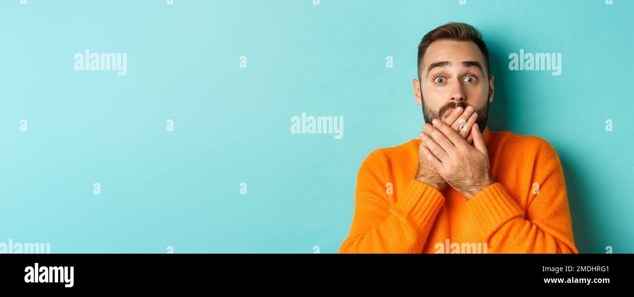 Close-up of shocked caucasian man covering his lips and mouth, staring ...