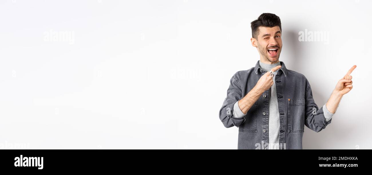 Handsome smiling guy making announcement, winking and pointing at upper ...
