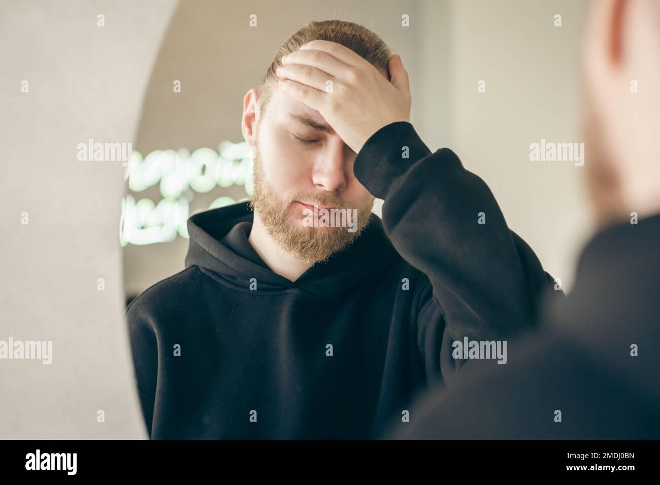 Sad young man with a beard in front of a mirror, mental health concept ...