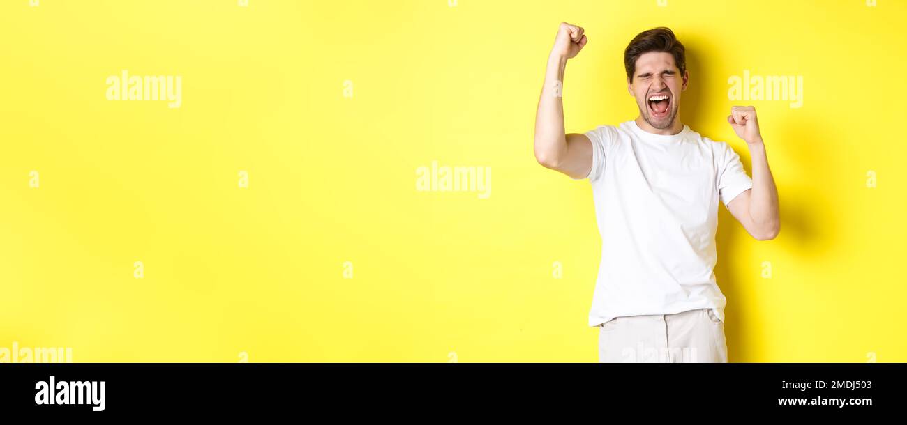 Excited handsome man winning and shouting for joy, raising hand up and ...