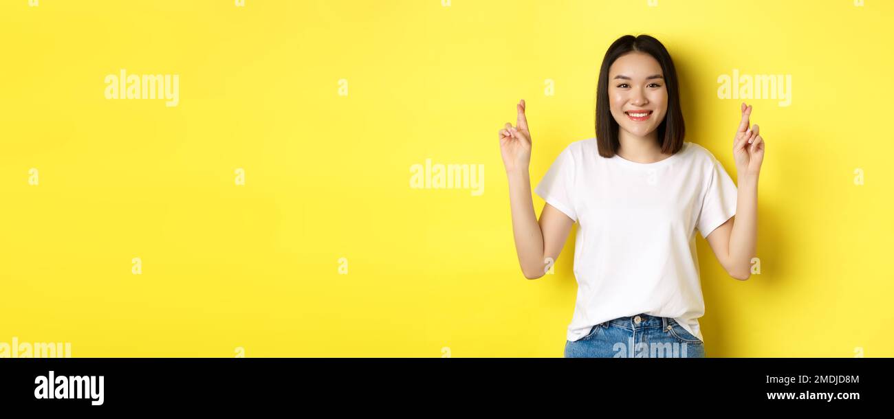 Hopeful asian girl making wish, cross fingers for good luck and praying ...