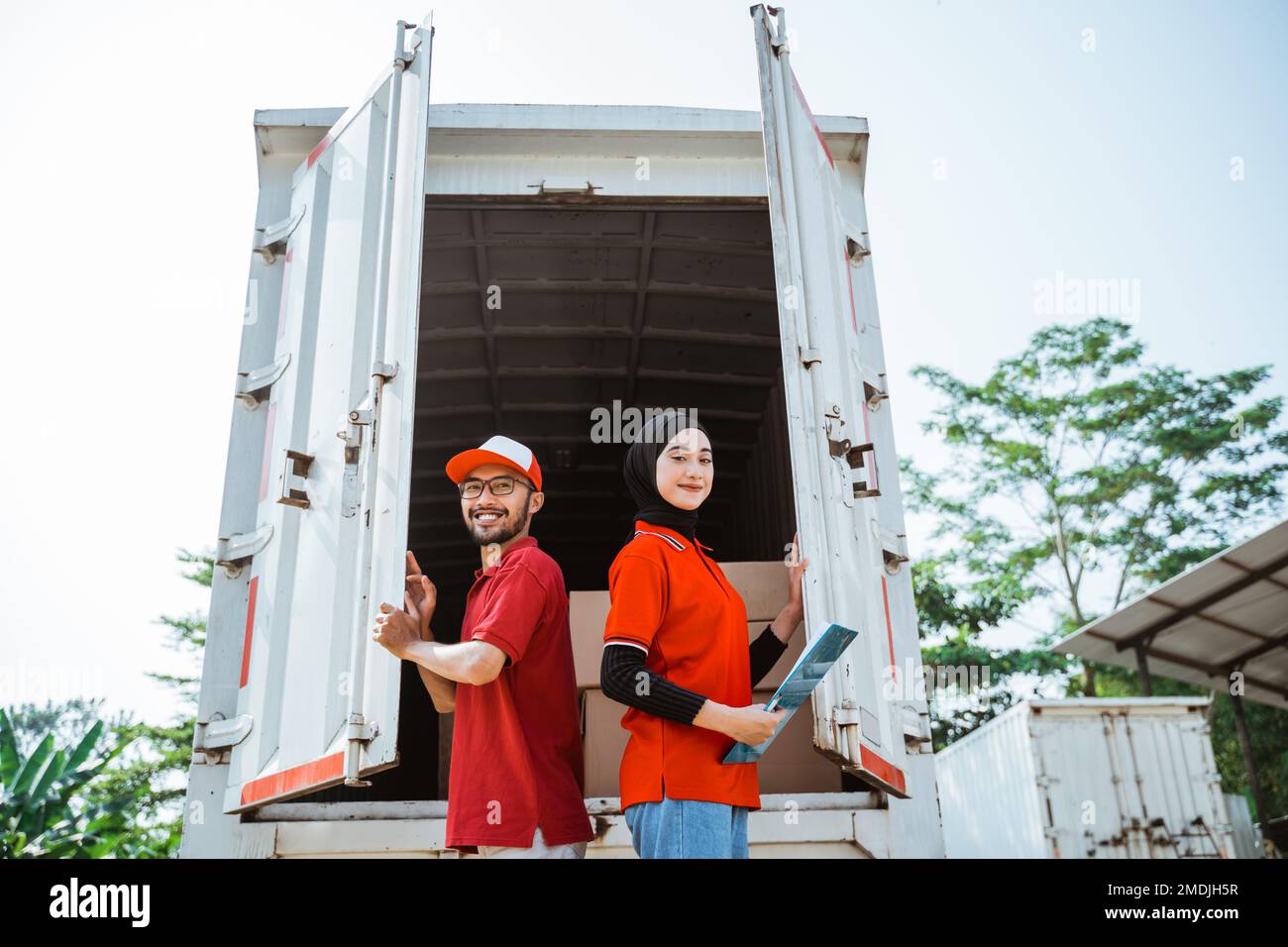 female worker holding clipboard with delivery man closing container ...
