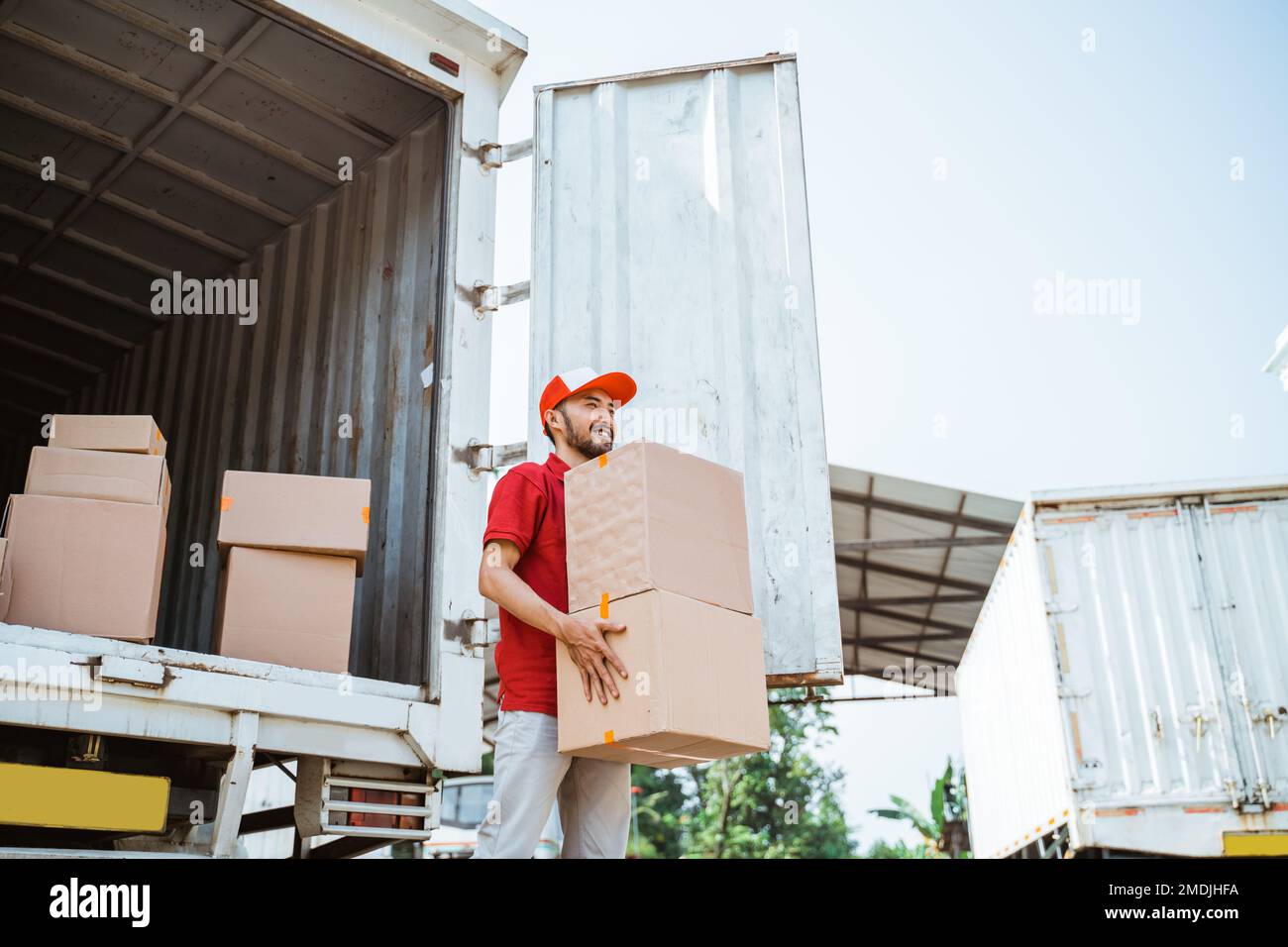 delivery man in red uniform lifting parcel box from container Stock ...