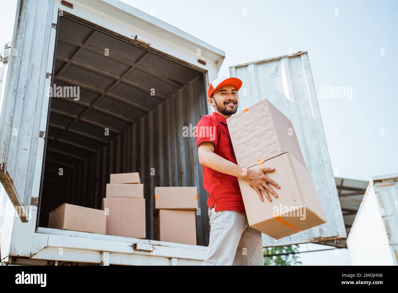 delivery man smiling while lifting parcel box against container ...