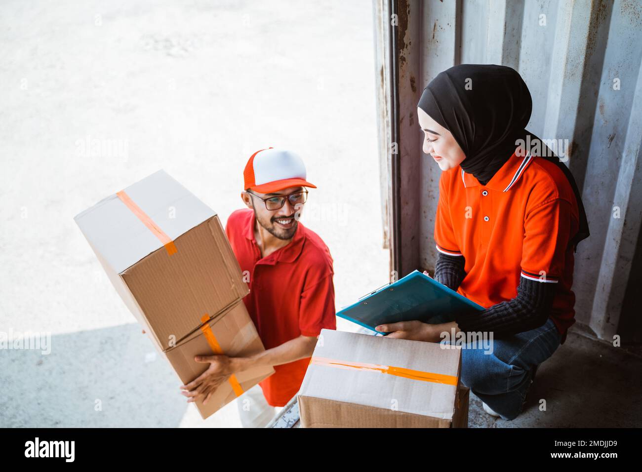male workers lifting boxes and women workers in headscarves checking ...