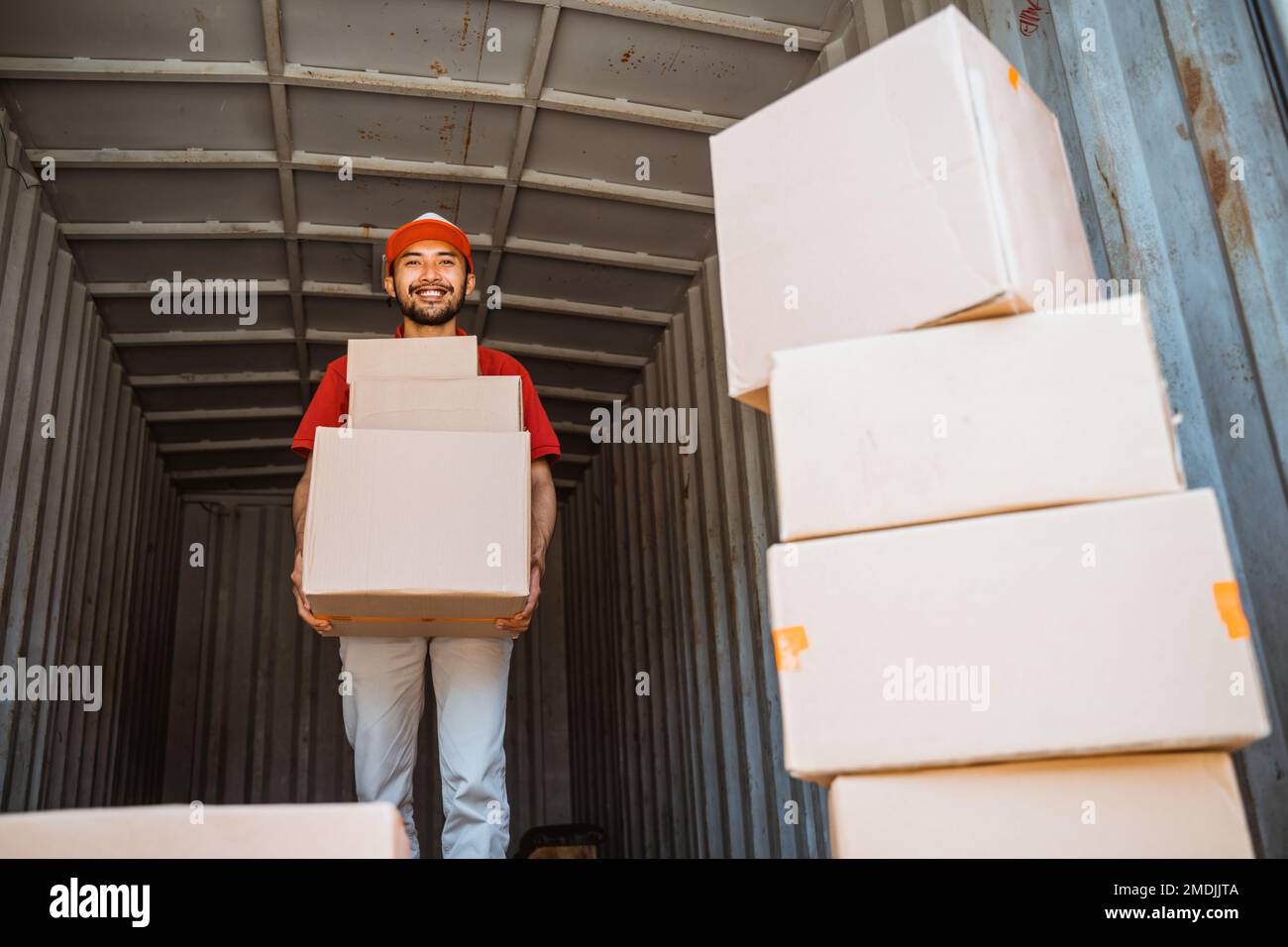 male employee in red uniform lifting packages in container truck Stock ...