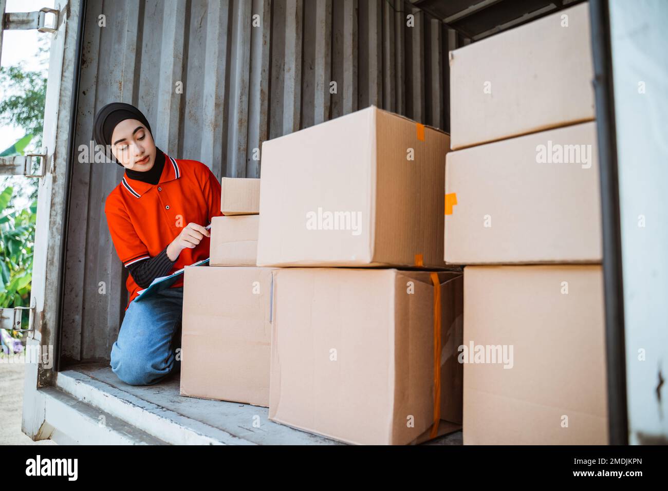 Hijab female employee carrying clipboard checking cardboard box in ...