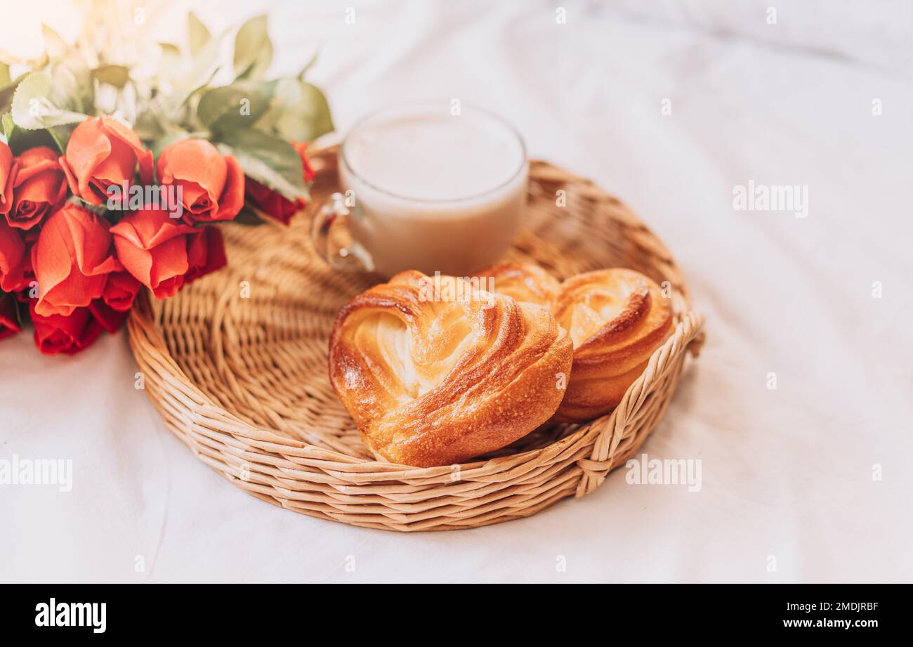 Wicker tray with pastries and coffee and flowers on white bed linen ...