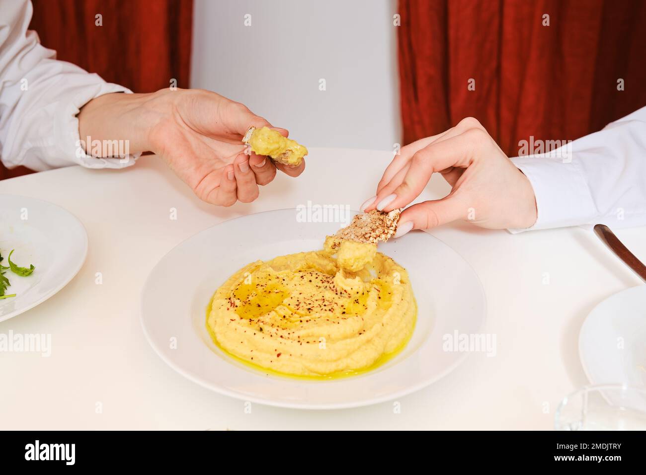 Two female hands dipping pieces of cracker into bowl with hummus Stock ...