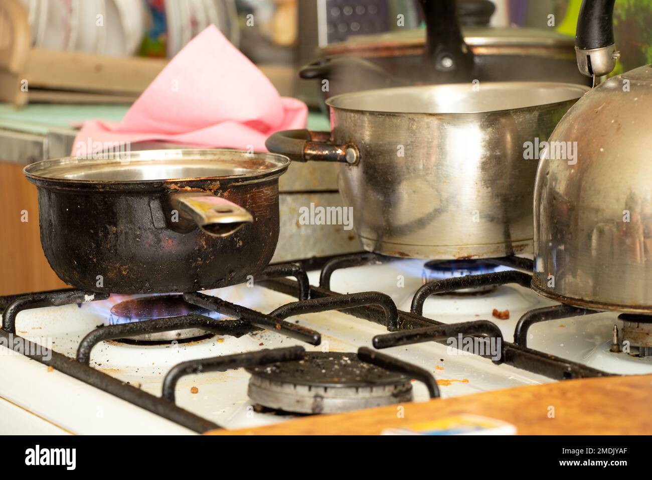a dirty saucepan stands on a dirty gas stove in the kitchen at home ...