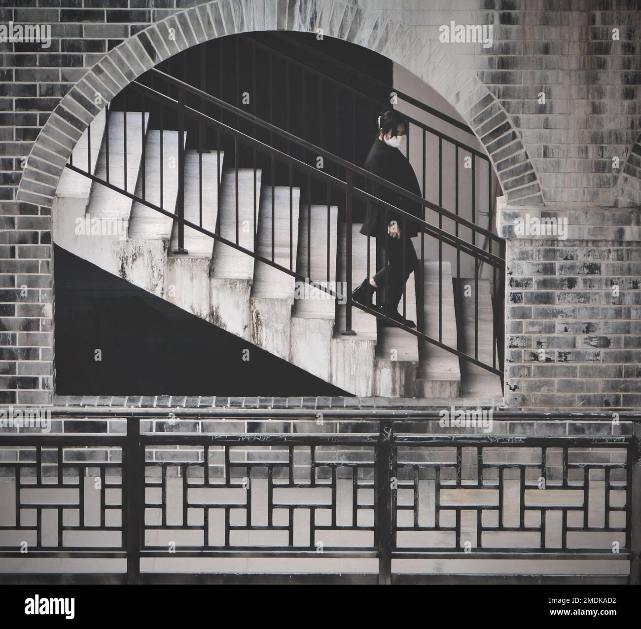 A side view of a woman with mask going downstairs seen behind arch ...