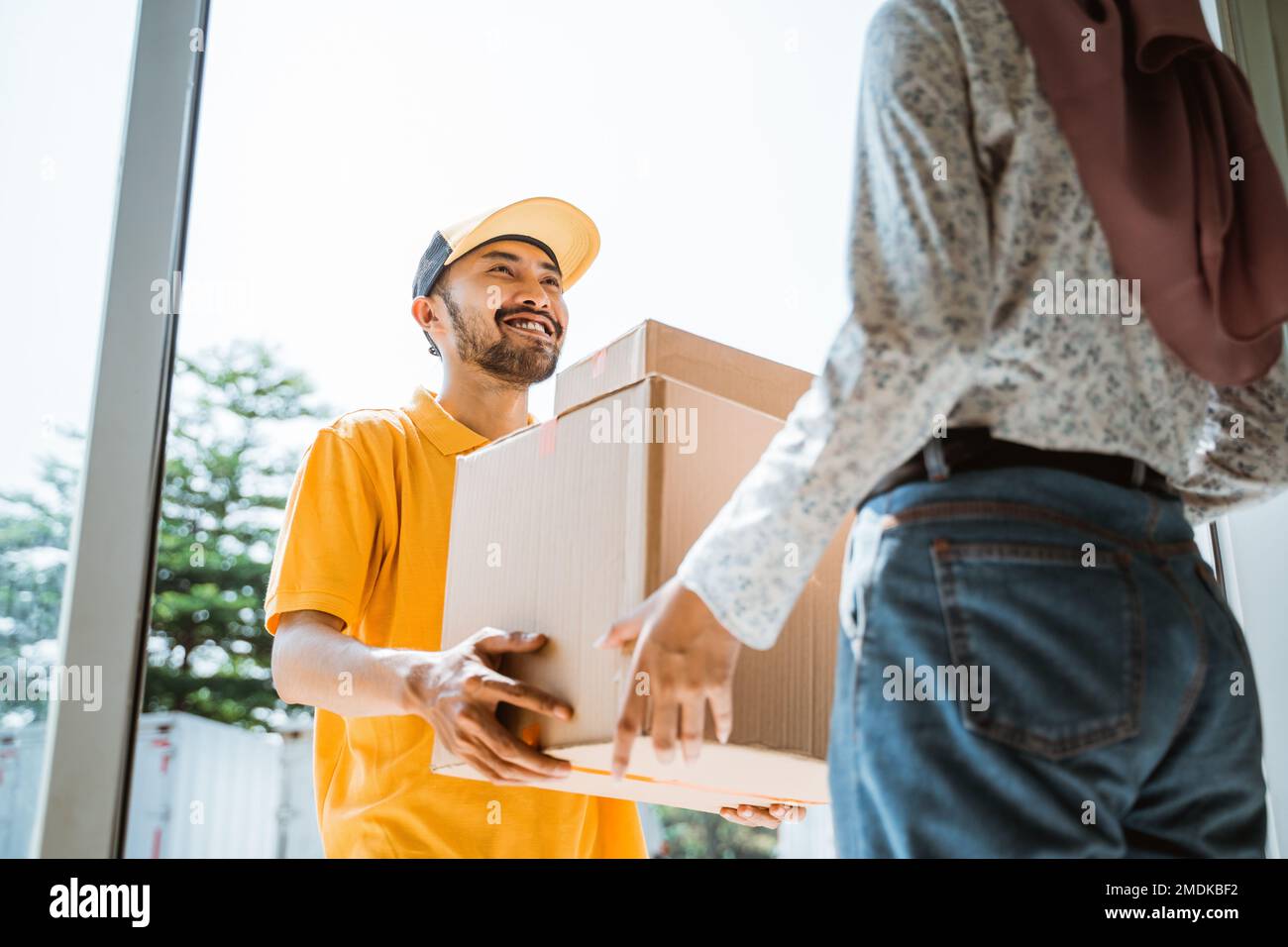 Bearded delivery man smiling friendly while handing box to customer ...