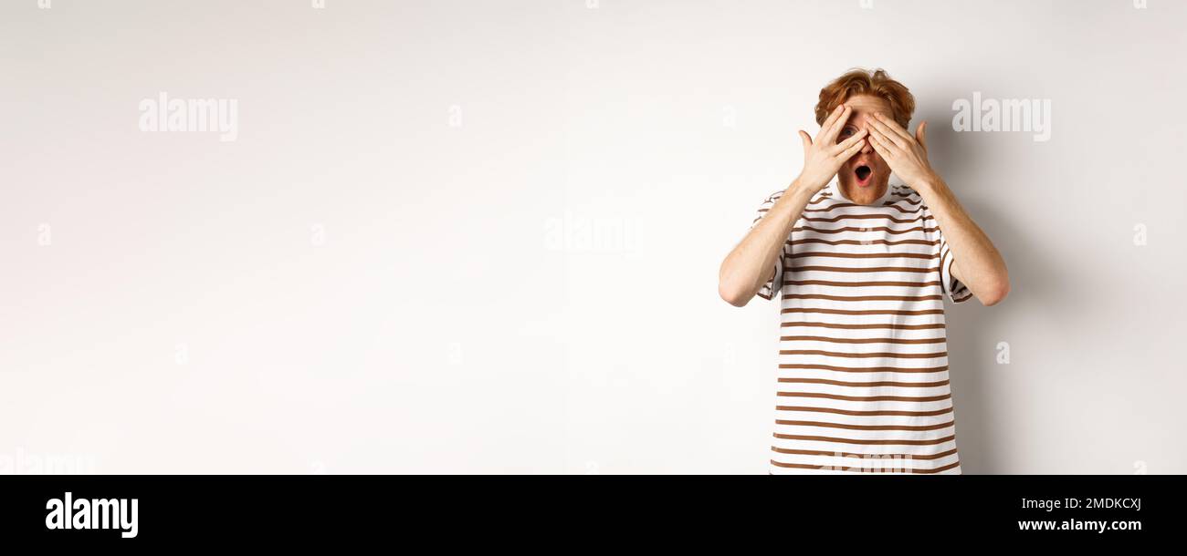 Shocked and embarrassed redhead guy covering eyes, peeking through ...