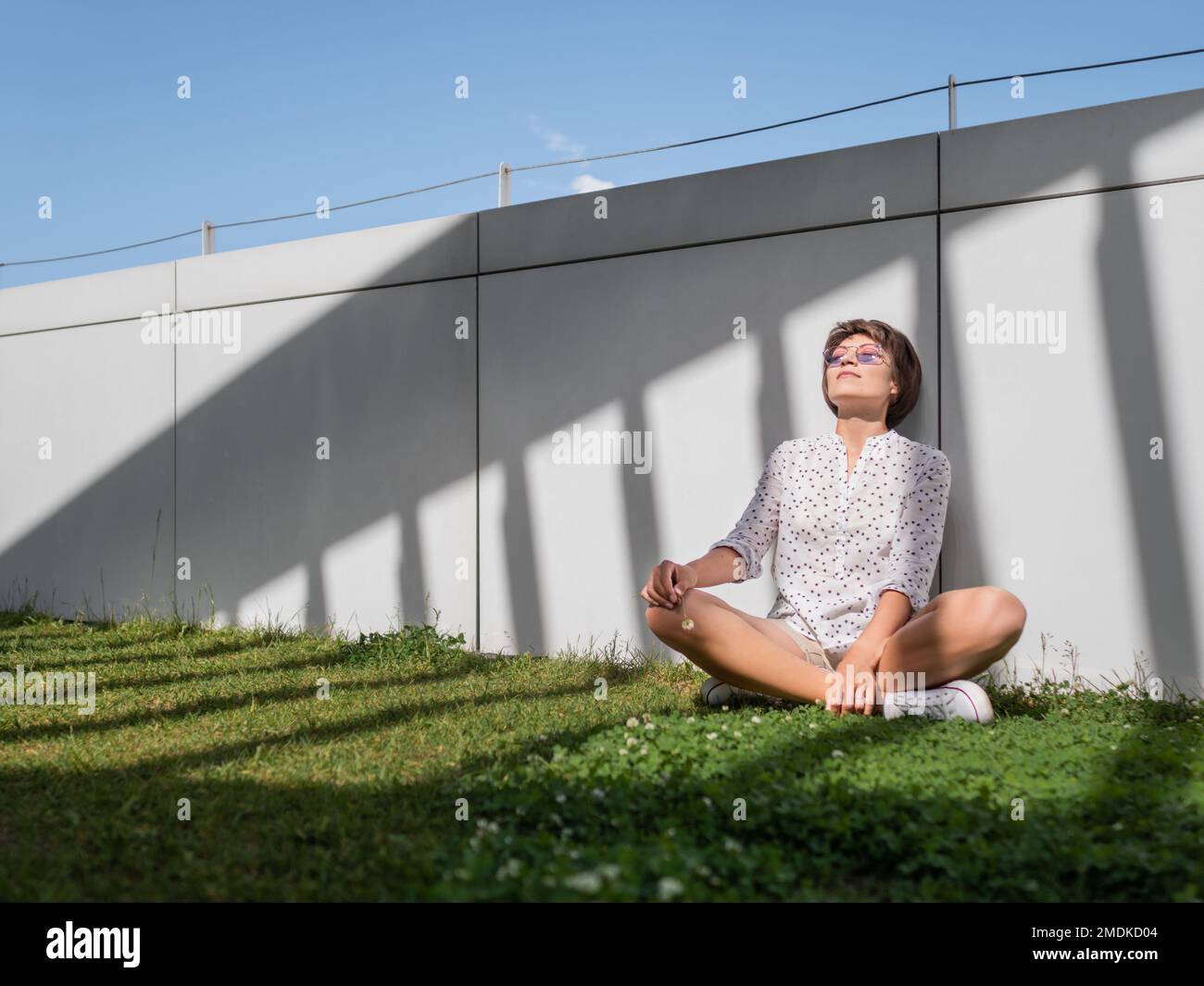 Mindful woman is meditating on lawn in urban park. Nature in town ...