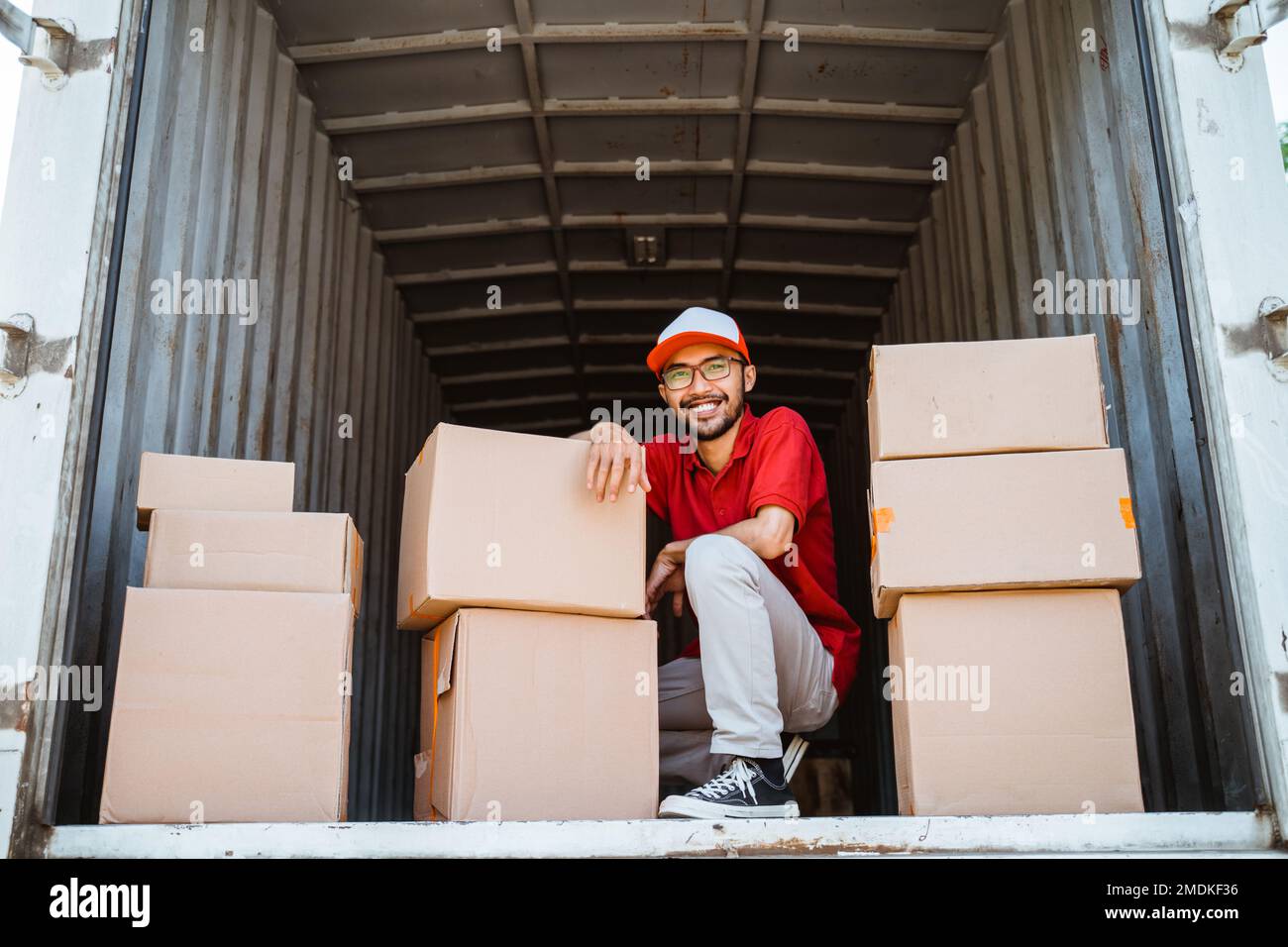 Smiling asian delivery man squatting between several packages Stock ...