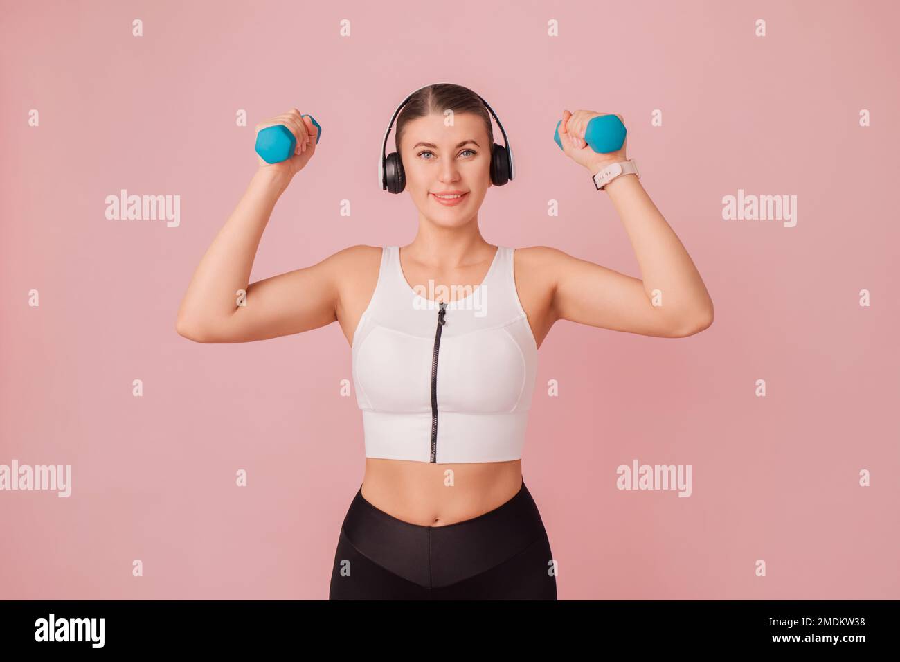 Smiling young woman in headphones doing sport exercise while standing ...
