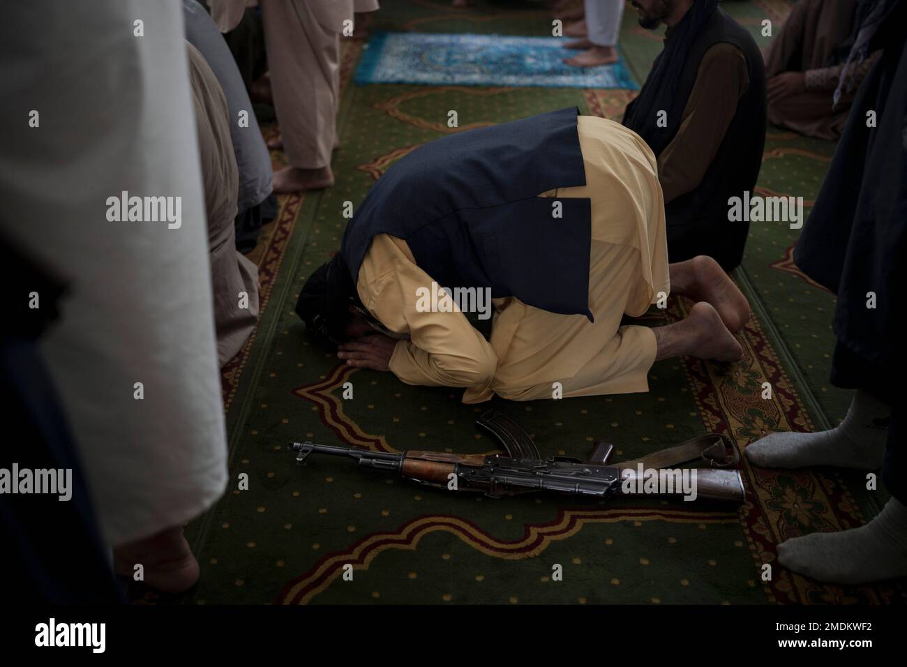 A man prays next to an AK-47 rifle of a Taliban fighter during Friday ...