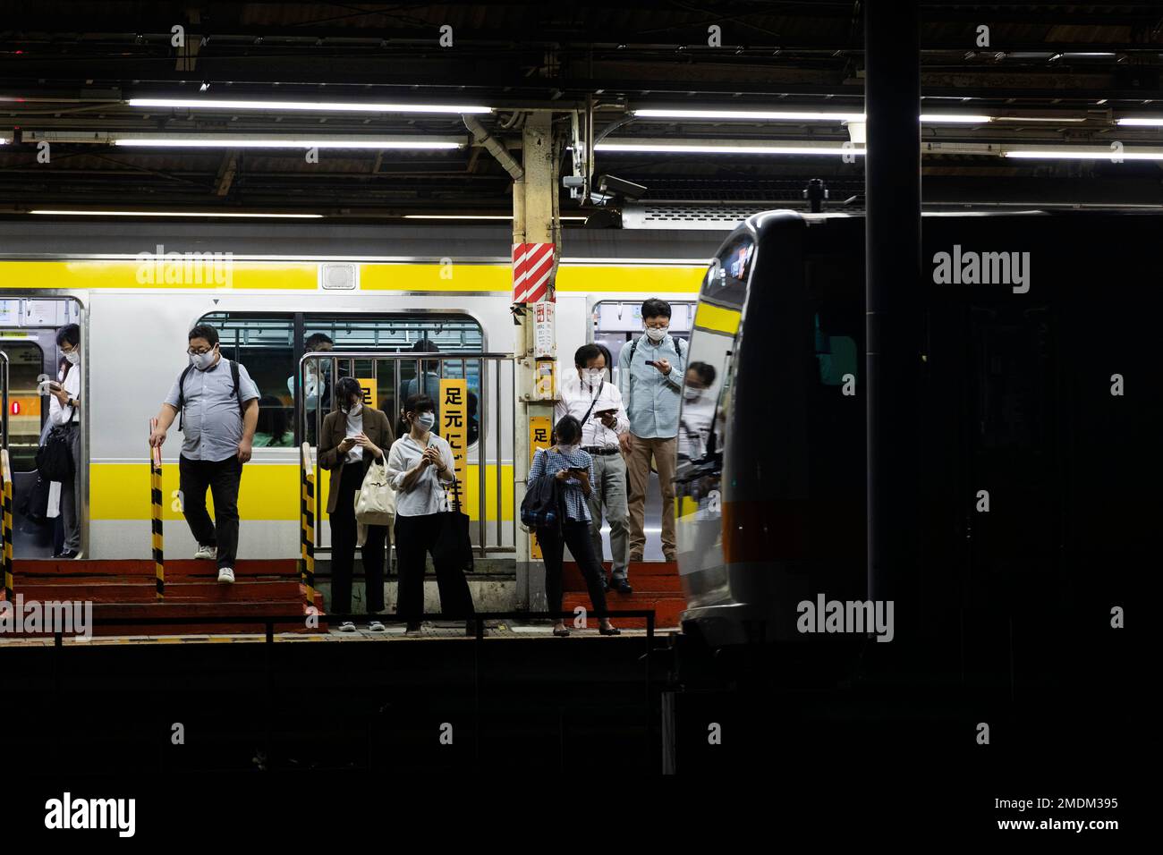 People wearing face masks wait for a train as it approaches at a ...
