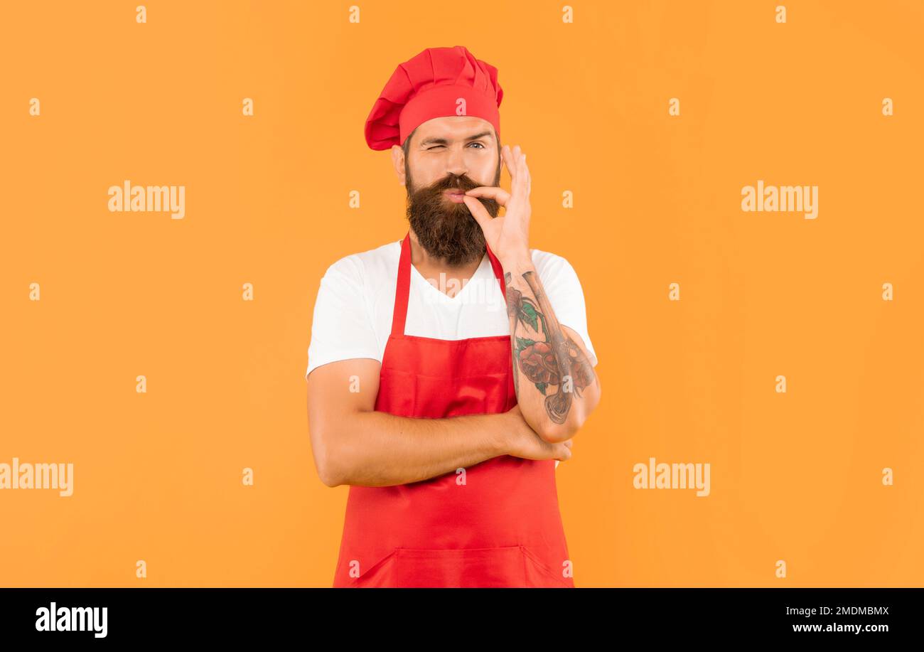 Winking man in red apron and toque licking finger yellow background ...
