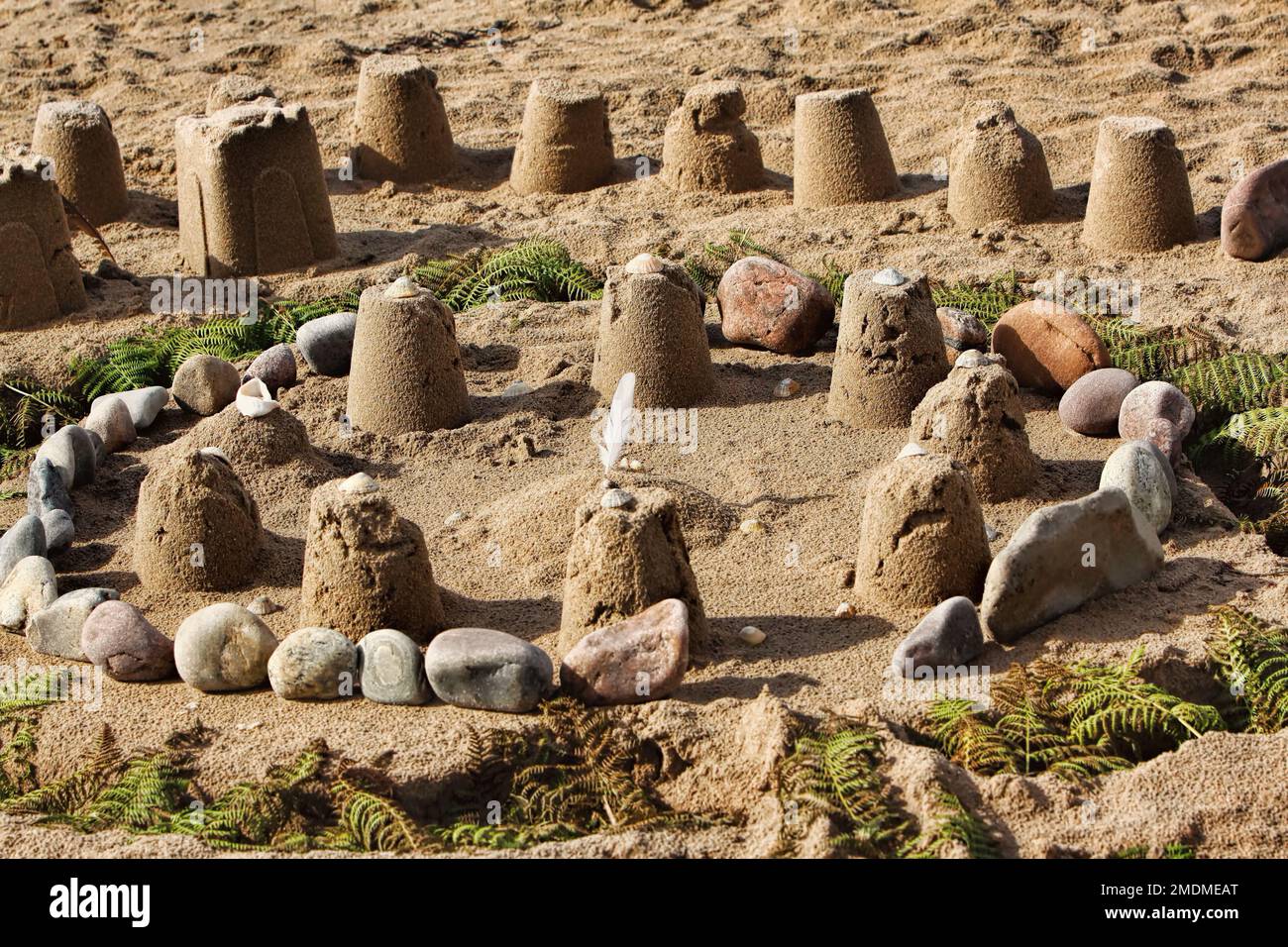 Sand castle fortress ringed with stones and with a white feather flag ...
