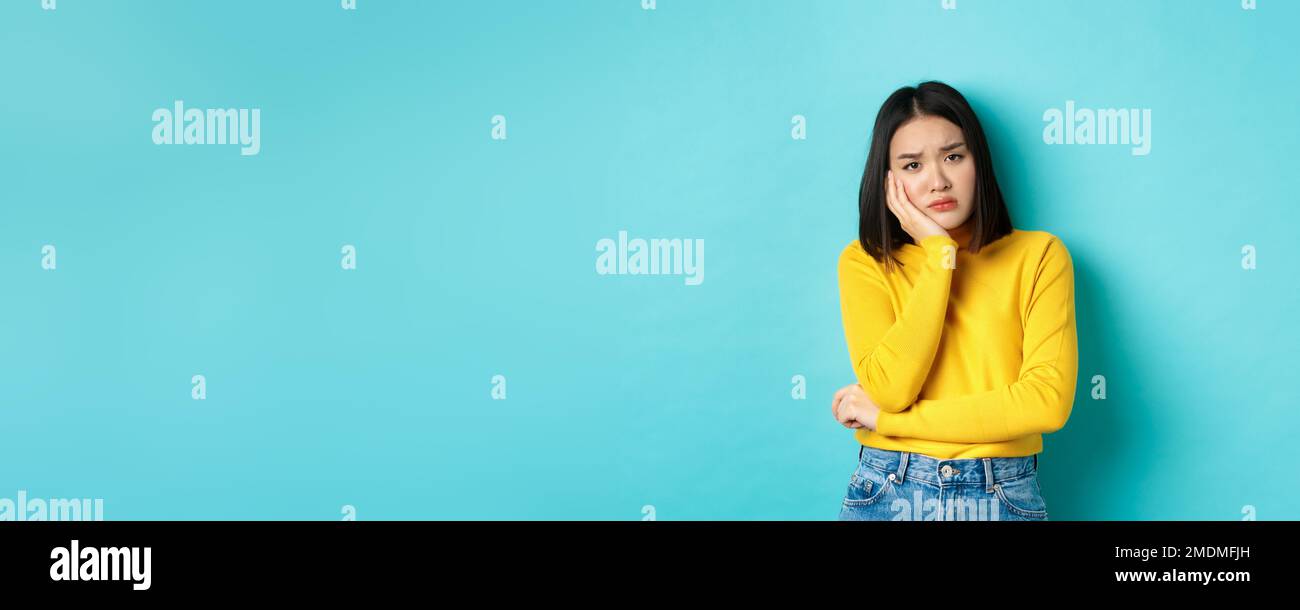 Sad and bored asian girl looking reluctant and unamused at camera ...