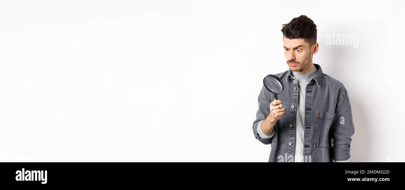 Serious man investigating, looking down with magnifying glass, stare ...