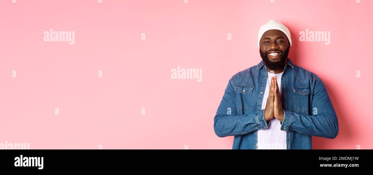 Happy smiling Black man saying thank you, holding hands in pray or ...