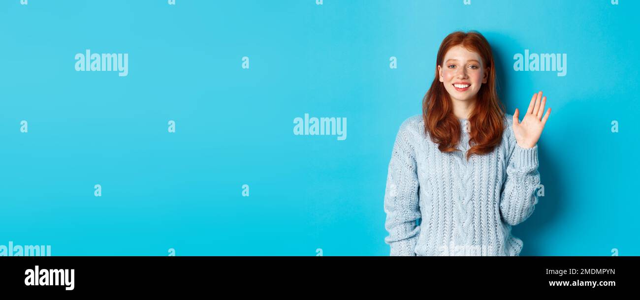 Friendly redhead teenage girl saying hi, waving hand in hello gesture ...