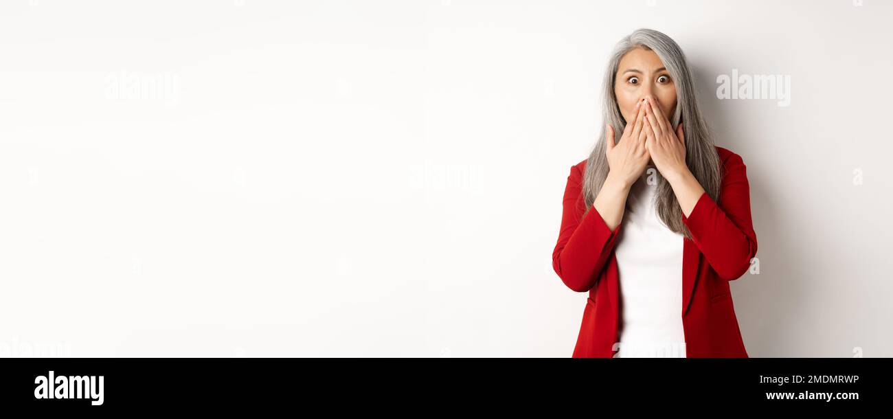 Shocked asian senior lady gasping, cover mouth from amazement, hear ...