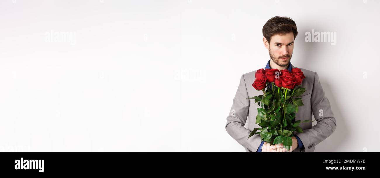 Handsome macho man going on date in suit, holding bouquet of red roses ...