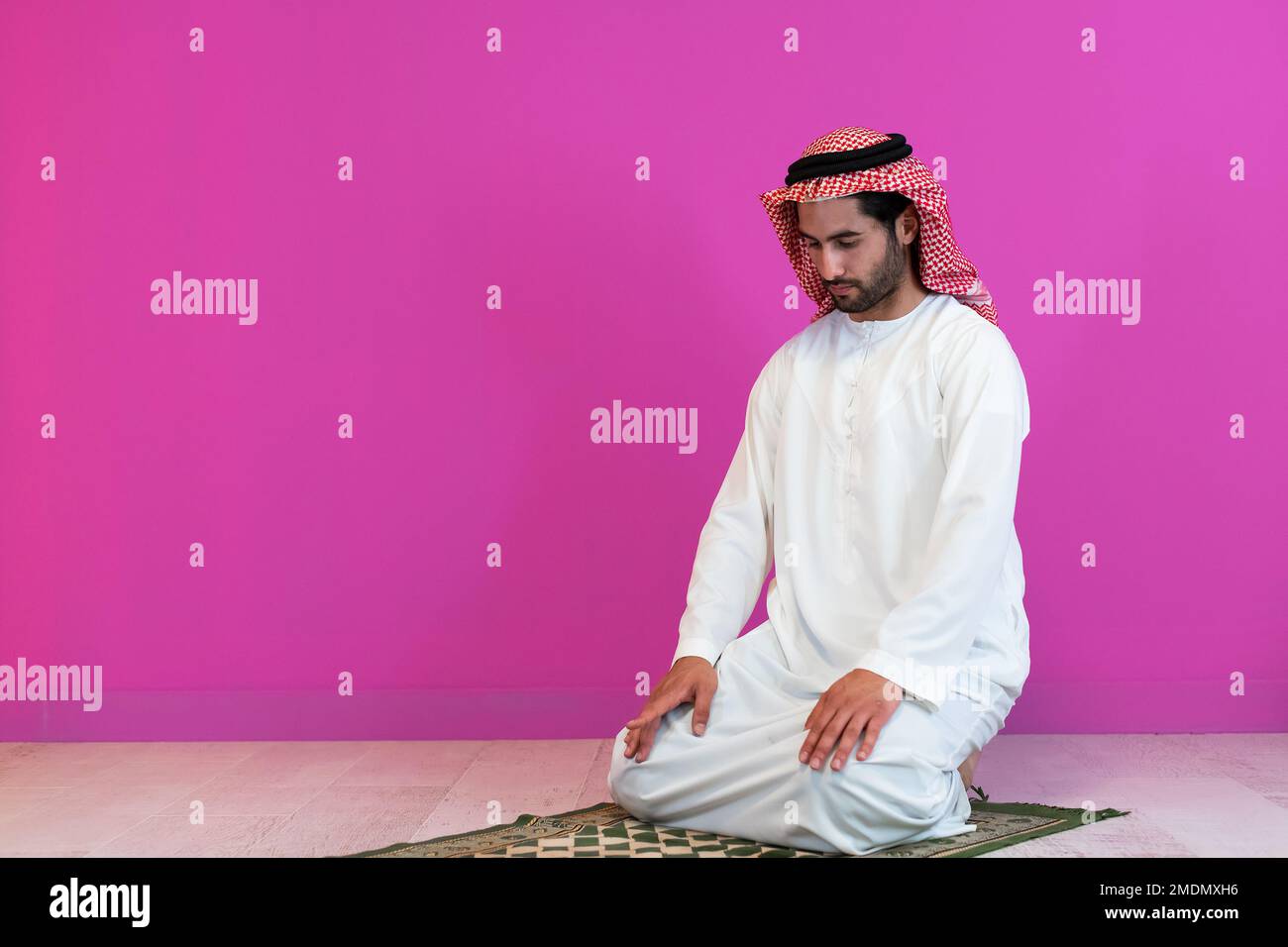 Young arabian muslim man in traditional clothes praying on the carpet ...